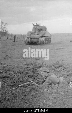 An infantryman shelters in a shell-hole as a Sherman tank advances ...