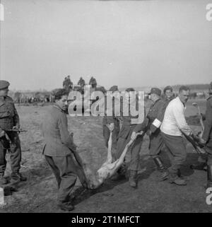 German SS guards carry the body of a deceased woman to a mass grave at ...