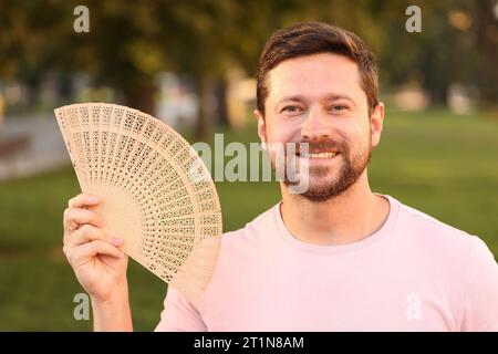 Happy man holding hand fan on light blue background Stock Photo - Alamy