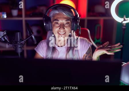 Middle age woman with tattoos playing video games wearing headphones ...