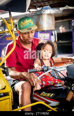 A Filipino father plays with his cute daughter sat on his tricycle ...