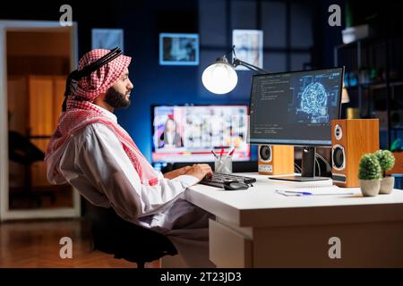 Muslim guy working with code and AI interface on a desktop computer. He ...