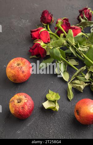 Withered, decaying, roses flowers and apples on black concrete ...