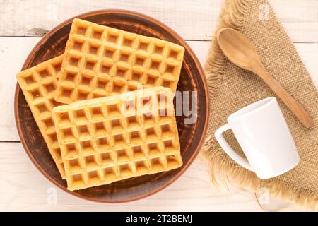 Plate with freshly baked waffles and cup of coffee on old wooden table ...