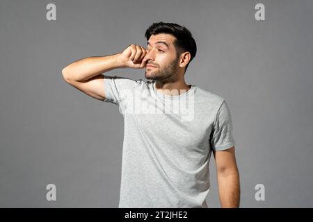 Weary bearded young man in white shirt sitting at table while tilting ...