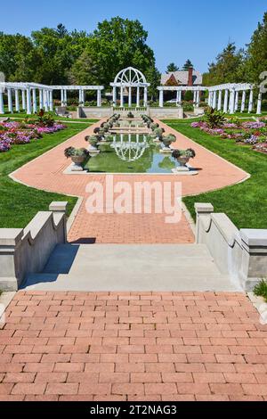 Brick pathway leading to pools of water and white pergola with ...