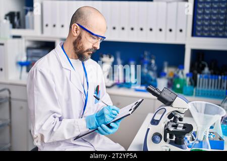 Young bald man scientist writing report working at laboratory Stock ...