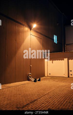 Spaceman sitting under lamp at a wall at night Stock Photo - Alamy