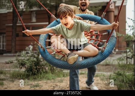 Parents swinging their smiling son in an urban park on an autumn day ...