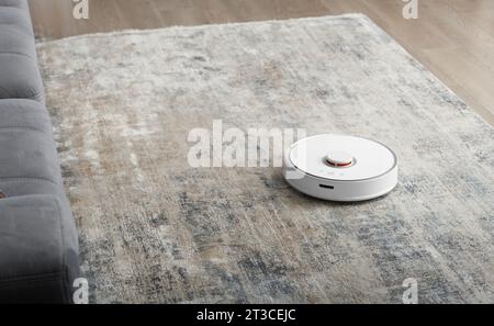 Modern robot vacuum cleaner near sofa in room Stock Photo - Alamy