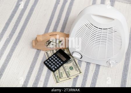 Money with electric fan heater and calculator on blue background ...