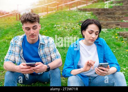 Sad couple using phones outdoors. A man peeping into a woman's phone ...