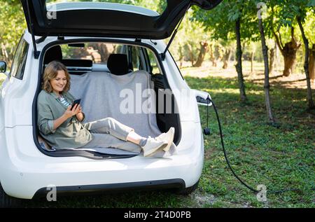 Woman with smartphone sits in an electric car's trunk Stock Photo - Alamy