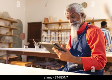 Focused biracial senior potter with long beard using potter's wheel in ...
