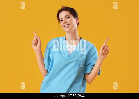 Female medical intern pointing at something on yellow background Stock ...