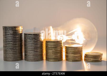 Light bulb lit with stacks of coins of descending height. Reduction in ...