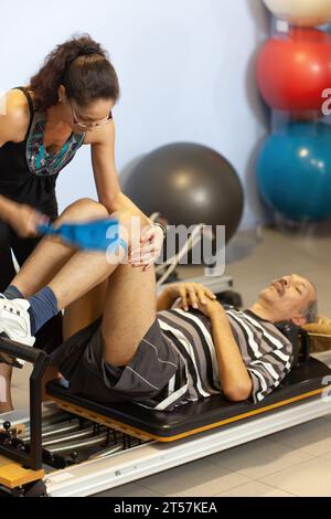 Woman pilates instructor helping senior man exercising on combo chair ...