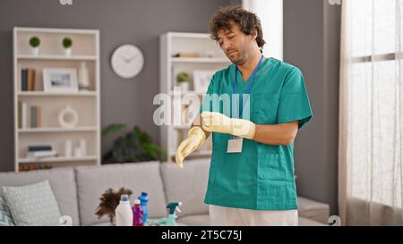 Young hispanic man wearing cleaner apron holding cleaning product ...
