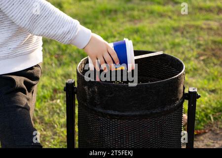 A child throws a plastic cup in the trash. Garbage recycling and ...