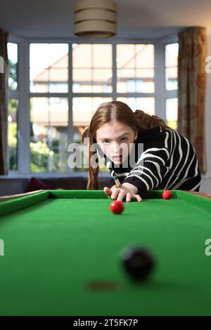 Teen girl playing bagatelle about to strike ball with cue in lounge at ...