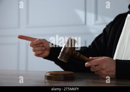 Judge with gavel pointing at wooden table against black background ...