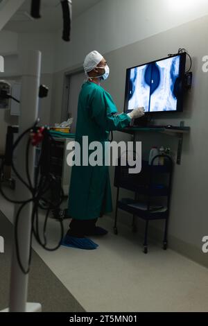 Biracial male surgeon looking at x-ray scans on screen in operating ...