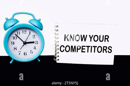 Notepad with text KNOW YOUR COMPETITORS with clock on white background ...
