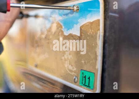 Using a screw driver to remove and replace a vehicle rear license plate ...