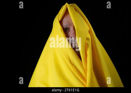 Bald, bearded man with a yellow cloth over his head against black ...