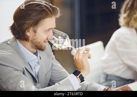 Successful looking male sommelier smelling and tasting white wine into ...