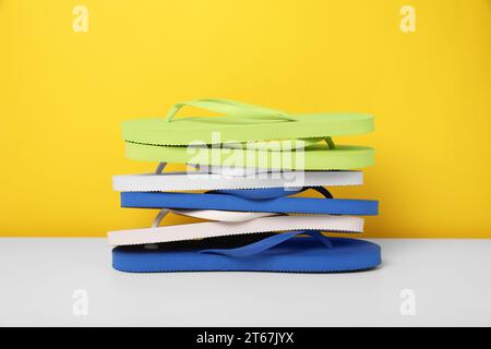 Stack of different flip flops on white table against yellow background ...