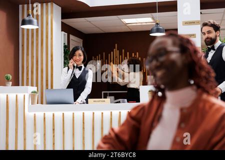 Asian receptionist making online booking using landline phone at ...