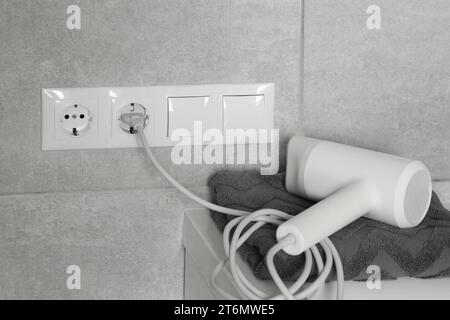 Hairdryer plugged into power socket on light grey wall in bathroom ...