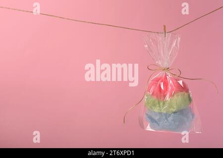 Packaged sweet cotton candy hanging on clothesline against pink ...