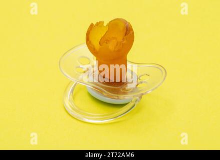 Low-quality torn baby silicone pacifier on a yellow background, close ...