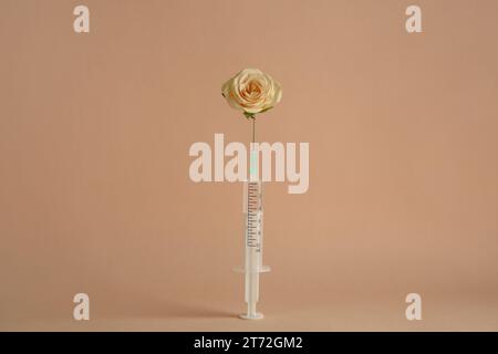 Medical syringe and rose flower on pale yellow background. Space for ...