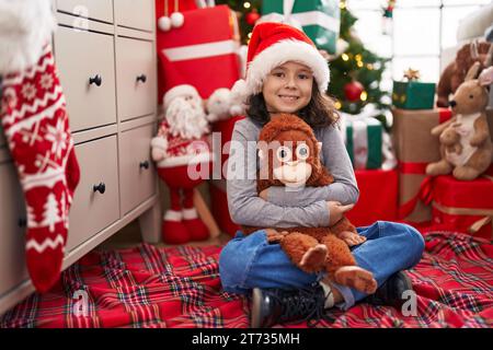 Adorable chinese girl hugging monkey doll sitting on floor by christmas ...