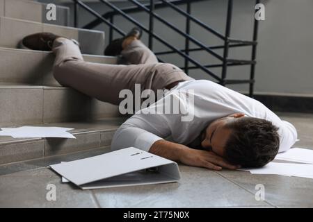Unconscious man with scattered folder and papers lying on floor after ...