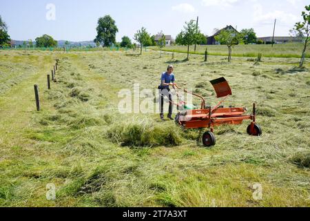 A rugged male farmer harvesting hay with a small tractor, pulling the ...