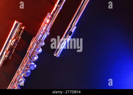 Disassembled metal flute isolated on dark table illuminated with red ...