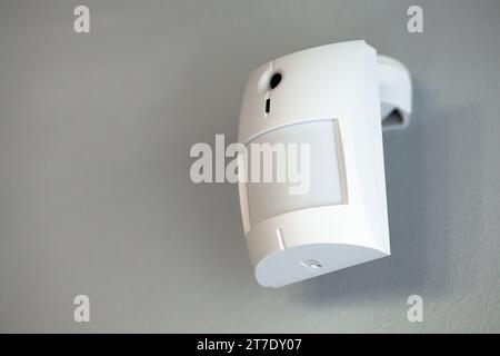 A white motion sensor camera on a gray wall, providing security and ...