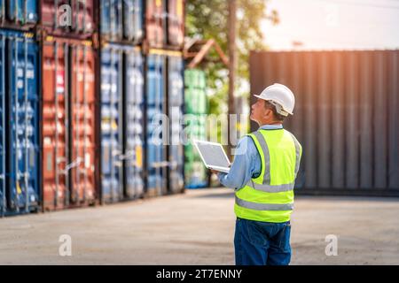 Engineer or foreman holding laptop and wears PPE checking container ...