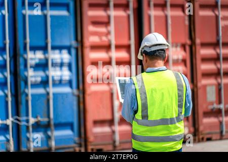 Engineer or foreman holding laptop and wears PPE checking container ...