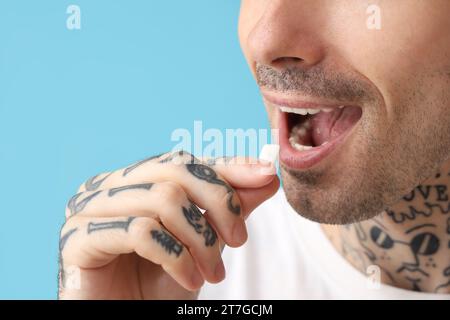 Young tattooed man with chewing gum on blue background, closeup Stock ...
