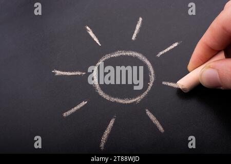 Hand drawing sun by chalk with light ray shape on blackboard background ...