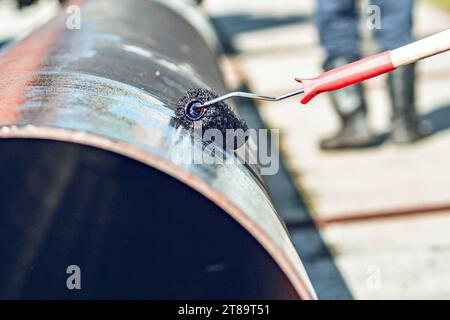 Metal pipe is painted with paint roller with black paint or bitumen ...
