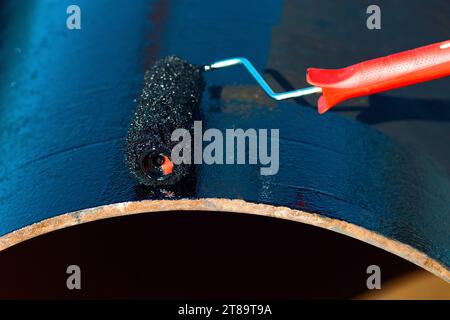 Metal pipe is painted with paint roller with black paint or bitumen ...