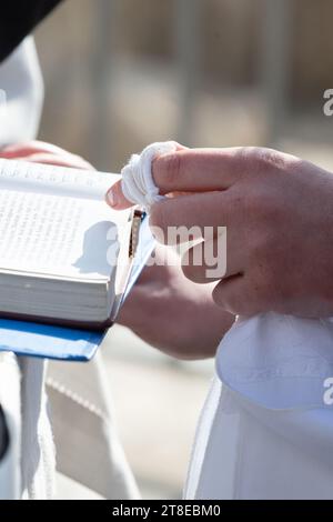 A hand gathers and holds the tzitzit, strings tied to the four corners ...