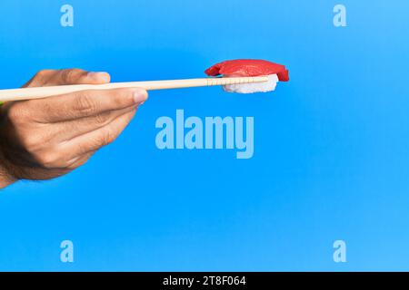 Hand of man holding tuna nigiri with chopsticks over isolated pink ...