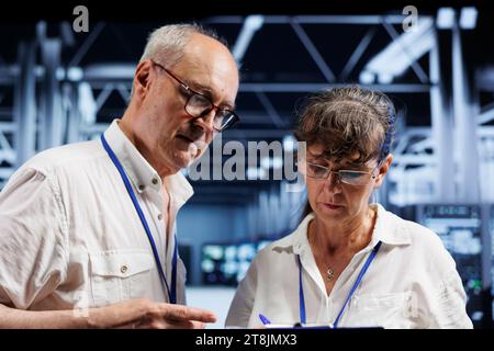 Elderly programmers in high tech workspace using mock up tablet to set up configuration ...